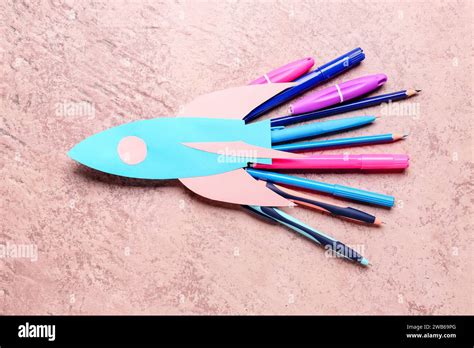 Blue Paper Rocket With Pens Pencils And Markers On Pink Grunge