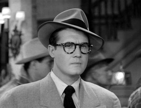 A Man Wearing Glasses And A Suit With A Hat On His Head Is Looking At