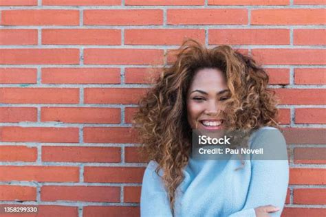 흰색 완벽한 미소 긴 곱슬 머리 매력적인 메이크업과 벽돌 벽에 포즈를 취하는 파란색 점퍼와 쾌활한 아프리카 계 미국인 여성 뷰티 우먼 라틴 민족 여성 얼굴 텍스트 공간 복사