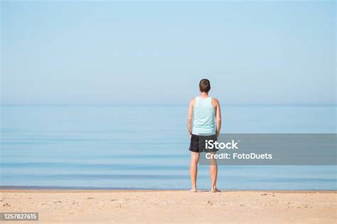 모래 위에 홀로 서서 따뜻한 여름 아침에 잔잔한 바다와 밝은 푸른 하늘을 응시하는 청년 정서적 긍정적 영감 텍스트 인용 또는 말을위한 빈 장소 다시 보기입니다 남자에 대한