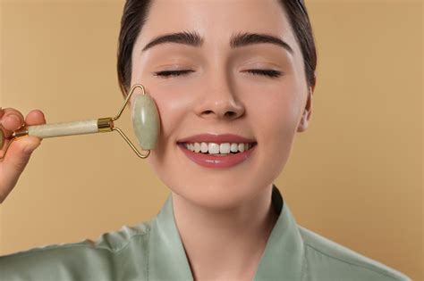 Young Woman Massaging Her Face With Jade Roller On Beige Background