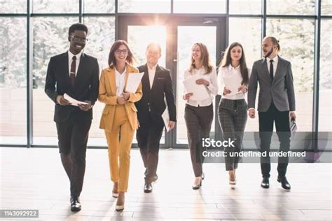 카메라를 향해 걷는 비즈니스 사람들 큰 창이 있는 현대 사무실에서 일 회의를 갖는 정장 복장의 행복한 젊은 사업가의 전체 길이 경영자에 대한 스톡 사진 및 기타 이미지