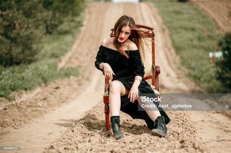 검은 드레스에 아름 다운 젊은 여자는 모래도로에 고전적인 안락의 자에 앉아 사진 작가를 위한 포즈 건강한 생활방식에 대한 스톡 사진 및 기타 이미지 Istock