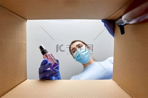 送货上门、运输和流行病概念 — 戴着防护性医用口罩和手套的女性打开装有化妆品和美容产品的包裹箱。高清摄影大图 千库网