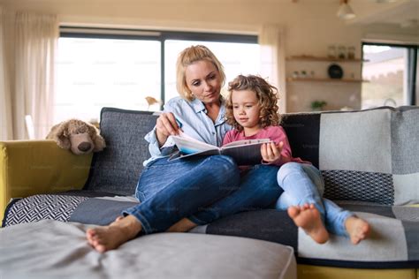 어머니와 함께 집 실내 소파에 앉아 동화책을 읽는 귀여운 소녀 사진 Unsplash의 맨발의 이미지