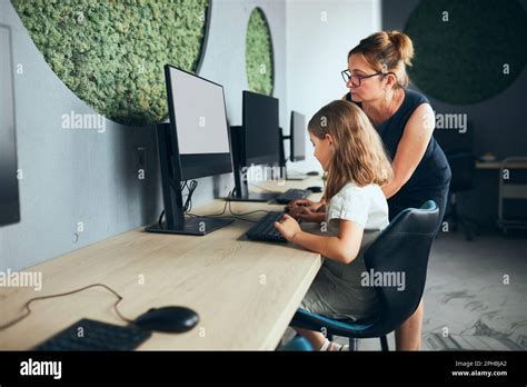 Teacher Assisting Schoolgirl While Computer Class At Primary School