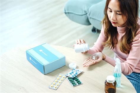 젊은 아시아 여성은 아프고 피곤하며 집에있는 거실에서 약을 복용 한 후 파란색 직물 소파와 담요에 앉아서 휴식을 취합니다 여자는