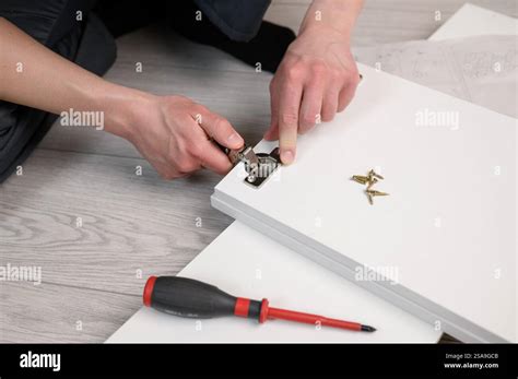 Assembling Furniture A Worker Inserts A Hinge Into A Wooden Closet