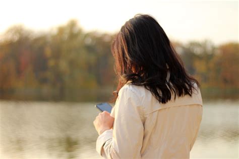 하얀 검은 머리 소녀는 휴대 전화를보고 가을 호수의 배경에 전화 화면에 손가락을 스 와이프 갈색 머리에 대한 스톡 사진 및 기타