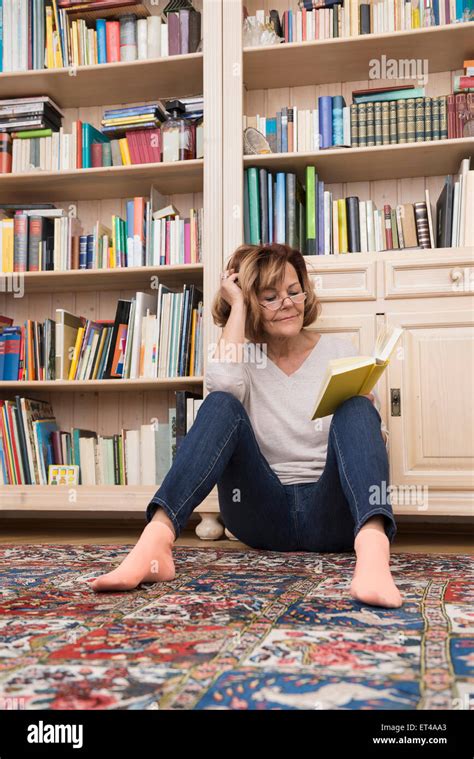Senior Woman Sitting On The Floor In Front Of Bookshelf And Reading