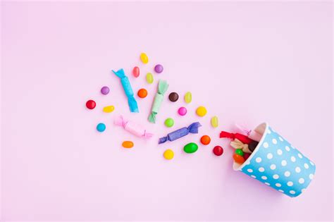분홍색 배경에 하얀 점이 있는 파란 종이컵에서 나온 다양한 종류의 다채로운 사탕 다양한 사탕 개체 그룹에 대한 스톡 사진 및