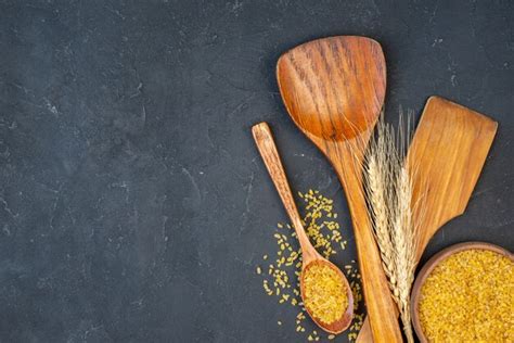 그릇에 있는 상위 뷰 Bulgur 밀과 나무 숟가락 두 개의 큰 나무 숟가락 밀 스파이크는 여유 공간이 있는 검은색 테이블에