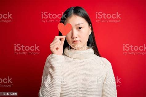 젊은 아시아 여자 들고 로맨틱 한 빨간 심장 종이 모양 위에 빨간 고립 된 배경 과 자신감 표정에 스마트 얼굴 생각 심각한