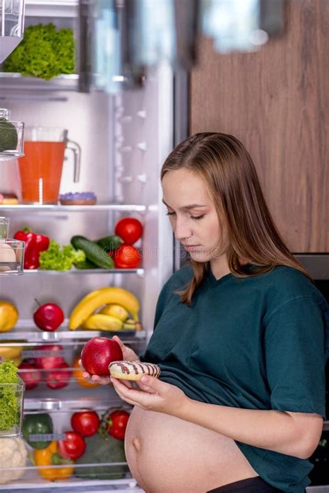 Pregnant Woman Near The Refrigerator Chooses What To Eat Between