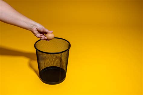 손은 닭고기 달걀을 쓰레기통에 던집니다 계란은 사무실 쓰레기통에 던져집니다 가금류 생산 문제 개념 0명에 대한 스톡 사진 및