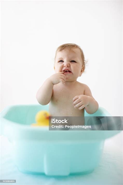 건강한 깨끗한 위생을 위해 몸을 씻는 동안 고무 오리로 목욕 시간을 즐기는 장난기 많은 아이 집에서 하얀 배경으로 욕조에 앉아있는 동안 손가락을 빨아 먹는 귀여운 아기 소녀