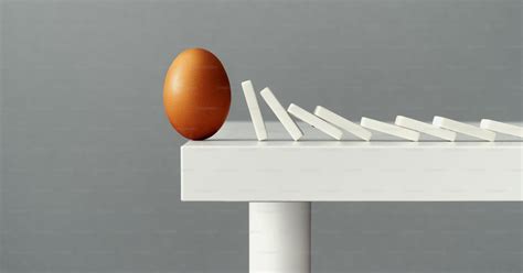 테이블 가장자리에서 균형을 잡는 계란 도미노 타일이 떨어지면서 떨어지고 부서지려고 합니다 사진 Unsplash의 도미노 이미지