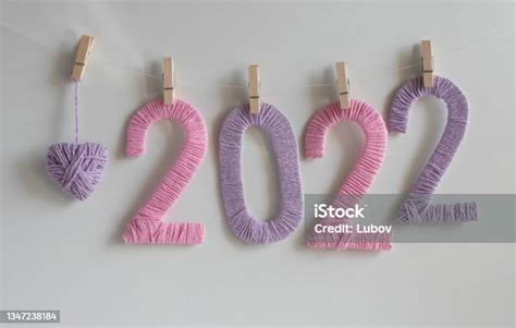 흰색 배경에 분홍색과 라일락 스레드로 만든 숫자 2022는 라일락 니트 하트 옆에 있는 옷핀에 매달려 있습니다 새해의 개념 12
