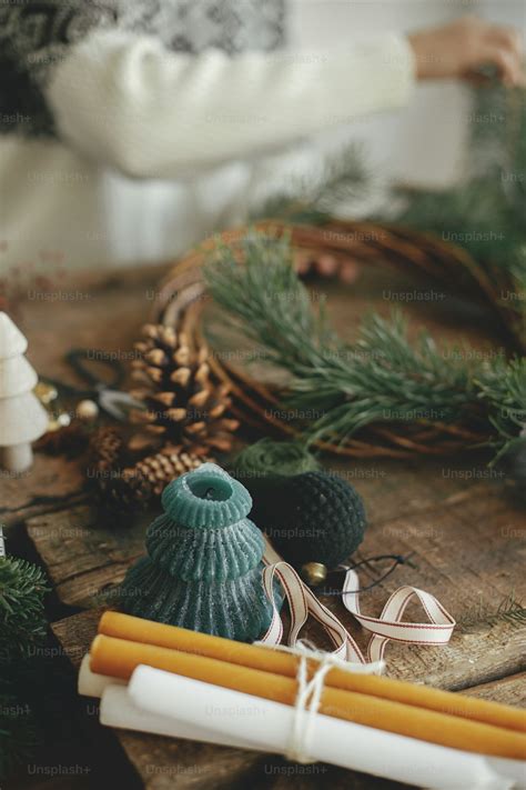 나뭇가지 브루니아 양초 가위 실 솔방울이 있는 소박한 나무 테이블에 세련된 현대적인 크리스마스 화환을 들고 있는 손 즐거운 성탄절 겨울 방학 준비 분위기