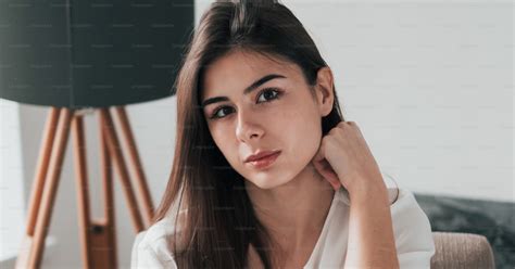 매력적인 여자가 회색 램프 근처의 의자에 앉아 있다 하얀 벽과 창문에서 나오는 일광이 있는 방에 있는 젊은 갈색 머리 사진 Unsplash의 우크라이나 이미지