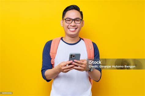 캐주얼 옷 배낭 안경을 쓴 젊은 아시아 남자 학생이 휴대전화를 손에 들고 노란색 배경에 고립되어 있다 고등학교 대학 대학 개념