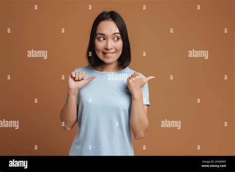 Young Asian Woman Biting Her Lip And Pointing Fingers Aside Isolated