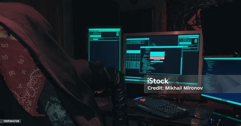 Hacker In A Hood Sits In Front Of Computer Screens And Hacks Databases