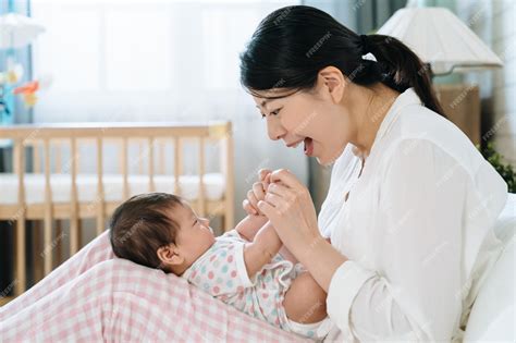 새로운 어머니로서 기쁨으로 가득 찬 아시아 여성의 초상화 아기의 손을 부드럽게 잡고 동요를 부르는 쾌활한 한국 엄마 어머니의