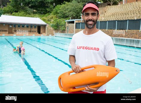 Portrait Of Lifeguard Standing With Rescue Buoy Near Poolside Stock