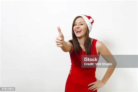 아름 다운 백인 젊은 행복 한 여자 빨간 드레스와 흰색 바탕에 엄지를 보여주는 크리스마스 모자를 착용 하는 매력적인 미소와 함께 산타 여자 격리 된 초상화입니다 새 해 휴일