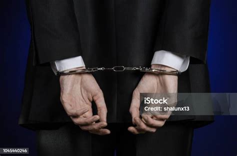 부패와 뇌물 테마 스튜디오에서 진한 파란색 배경에 그의 손에 수 갑과 검은 양복에 사업가 절연 뒤에서 보기 남자 사업가에 대한