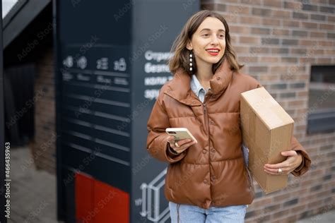 Babe Caucasian Woman With Parcel Near Automatic Post Terminal Smiling Girl Holding Smartphone