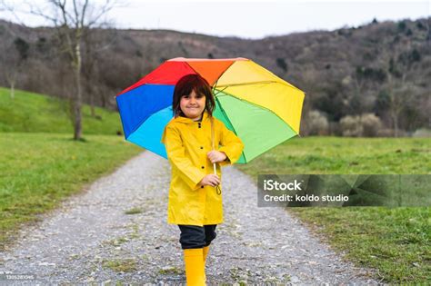 노란 비옷 노란 레인 부츠를 입고 목초지나 숲 길을 가로질러 미소짓는 어린 소년은 형형색색의 무지개 우산을 손에 들고 있다 4 5세에 대한 스톡 사진 및 기타 이미지