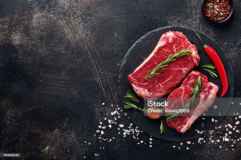 오래된 어두운 돌 배경에 양피지 종이에 로즈마리와 향신료와 두 개의 원시 스테이크 뉴욕 맨 위 보기입니다 모의 갈비 음식에 대한