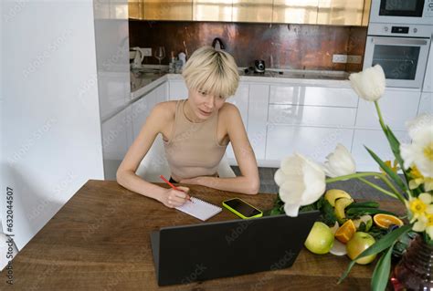 Curious Nutritionist Talking Diet Notes From Laptop In Kitchen Stock