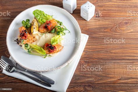 셀러리와 감자 퓌레에 붉은 생선 조각을 더하고 허브와 신선한 오이로 장식합니다 레몬 슬라이스와 흰색 접시에 나무 테이블에 0명에