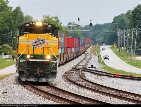 A Yellow Train Traveling Down Tracks Next To A Lush Green Field And