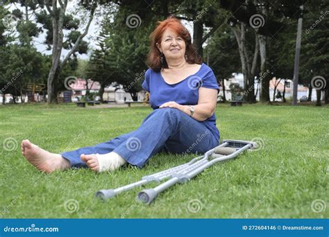 Woman Sitting On The Grass With A Bandaged Foot And Crutches At Her