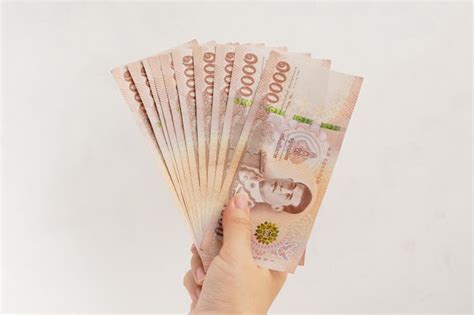 흰색 벽 배경에 새로운 1000 태국 바트 지폐를 들고 있는 손 비즈니스 및 금융 개념 프리미엄 사진
