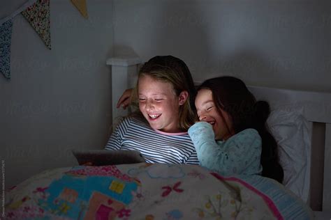 Young Girls Giggling Together Watching Movies At Bedtime By Stocksy