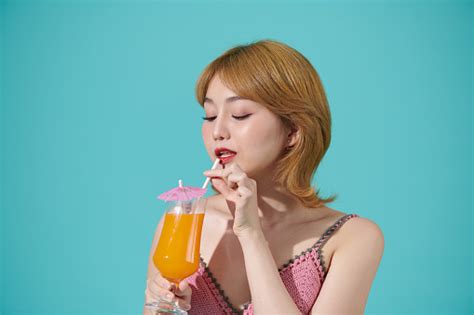 선글라스를 착용한 초상화 아시아 젊은 여성이 쾌활하게 웃고 여름에 오렌지 주스 한 잔을 들고 고립된 Nturquoise 배경