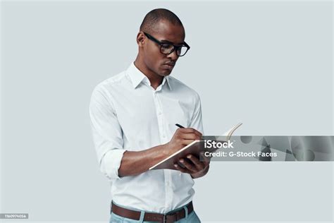 모든 것을 기록하려고 합니다 회색 배경에 서 있는 동안 아래로 뭔가 쓰기 잘 생긴 젊은 아프리카 남자 검은색에 대한 스톡 사진