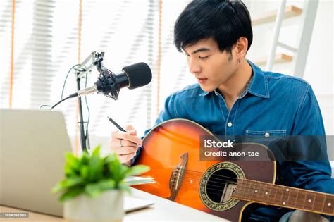 아시아 청년 작곡가는 어쿠스틱 기타를 연주하고 스마트 폰에서 노래를 듣고 생각 하 고 종이 가사 노래 홈 스튜디오의 거실에 앉아