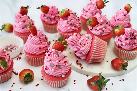 종이 케이크 케이스에 수제 핑크 벨벳 딸기 컵 케이크의 배치의 이미지 핑크 버터 착빙 파이프 소용돌이에 딸기 설탕 공예 심장 모양과 구 뿌리 측면에 누워 하나의 컵 케이크