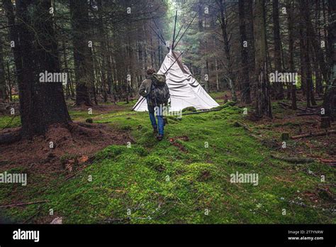 Rear View Of Man Walking With Rucksack Towards Tipi Tent In Nature And Forest Landscape Stock