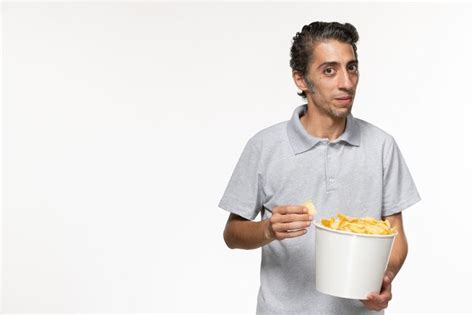 Jovem Macho Comendo Batata Frita Na Superfície Branca Foto Grátis