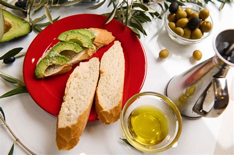 정물화 향신료를 뿌린 아보카도 조각을 곁들인 갓 구운 빵 조각 엑스트라 버진 올리브 오일 올리브 나무 가지로 둘러싸인 흰색 테이블의 금속 디캔터 옆 유리 그릇에 담겨