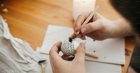 나무 테이블의 배경에 뜨거운 왁스로 부활절 달걀을 그리는 손 세련된 왁스 장식품이 있는 현대 부활절 달걀 행복한 부활절