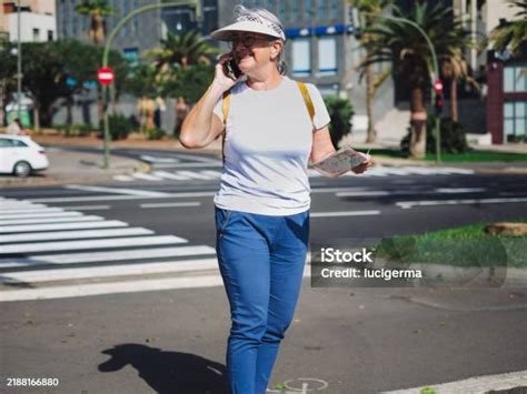 활동적인 노인 관광 여성은 캐주얼 한 옷을 입고 휴대 전화와지도를 들고 도시 거리를 건너 걷고 도시 생활을 배경으로 합니다 70 79세에 대한 스톡 사진 및 기타 이미지