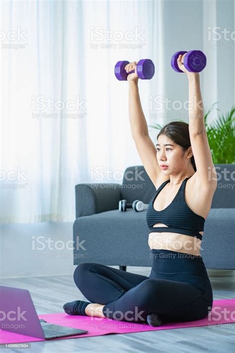거실에서 집에서 노트북으로 어깨 스트레칭 요가 온라인 수업을하는 웃는 아시아 여성 자기 격리 및 그 옆에 소파와 노트북과 함께